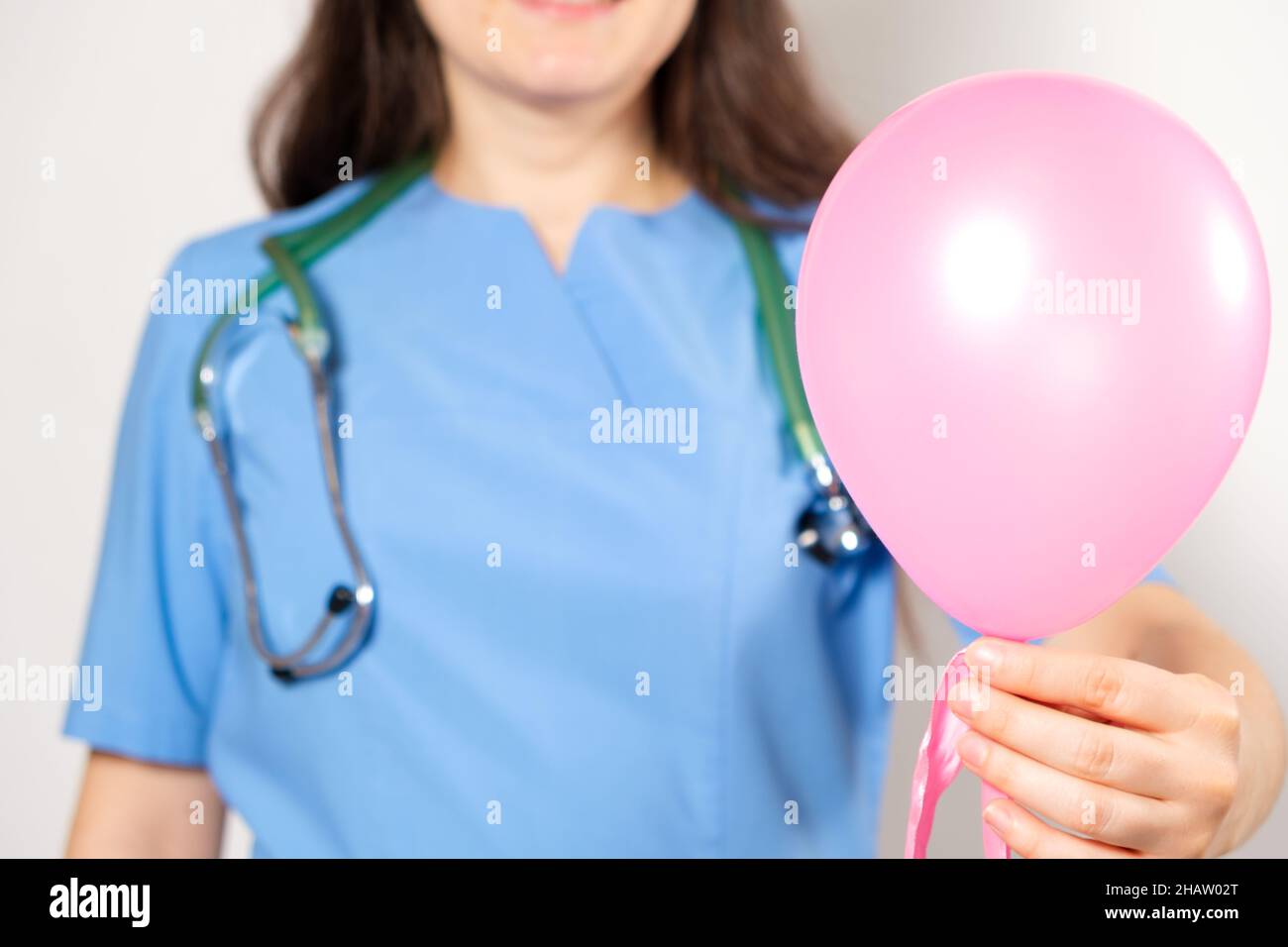 A doctor or nurse in a blue uniform holds a pink balloon with place for ...