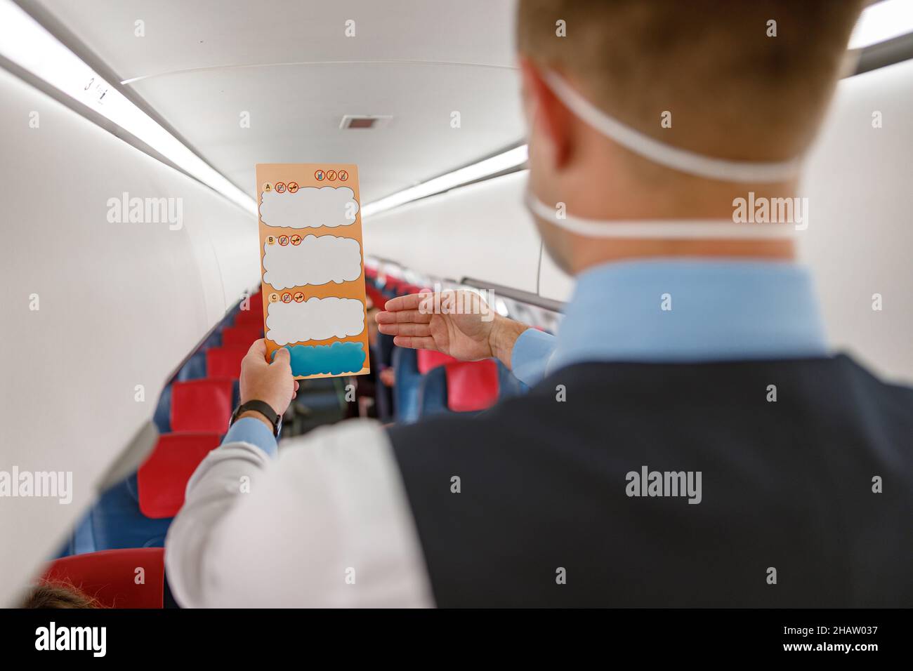Male flight attendant with paper booklet standing in airplane salon ...