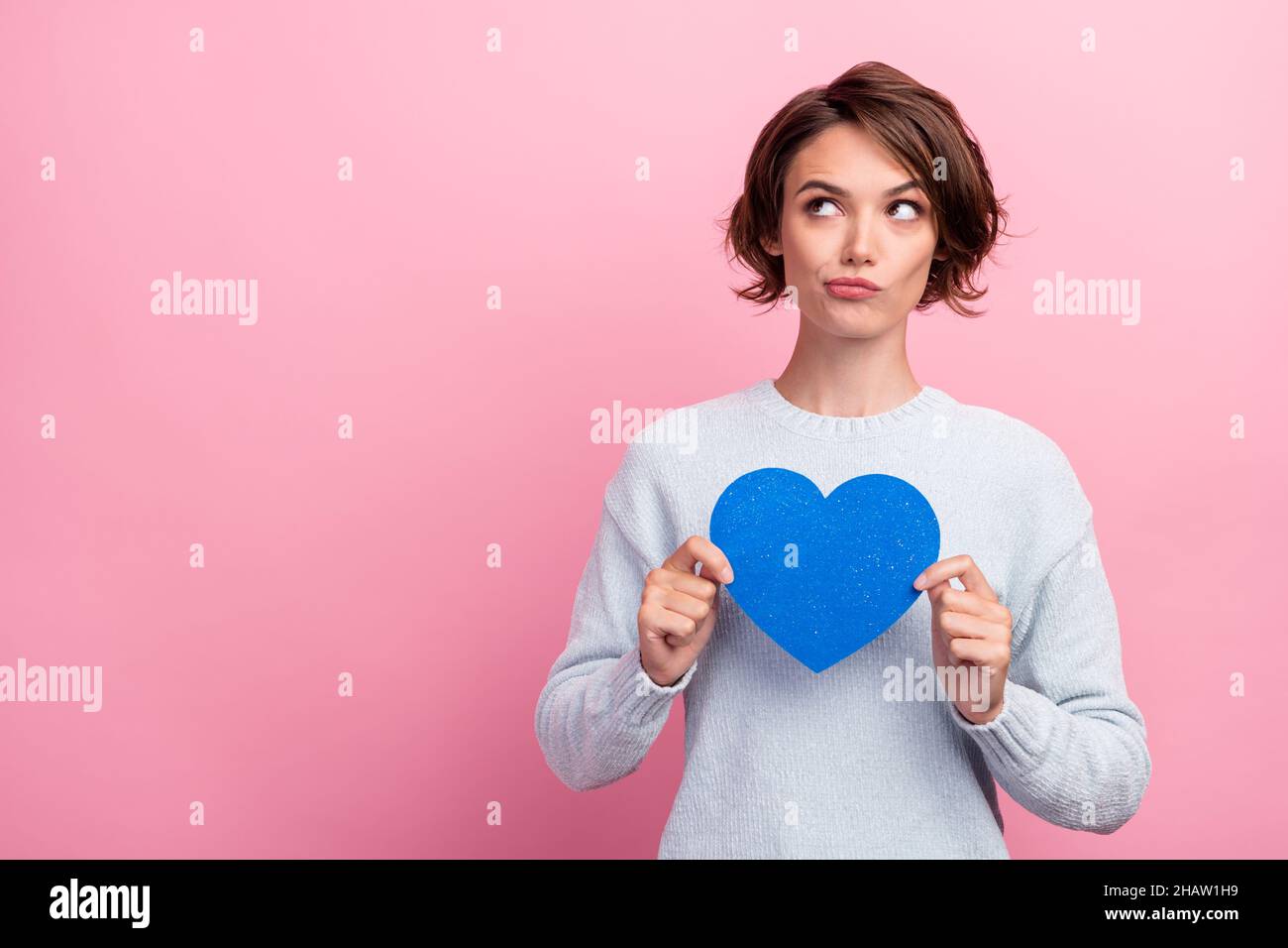 Photo of minded doubtful young woman hold blue heart paper shape ...