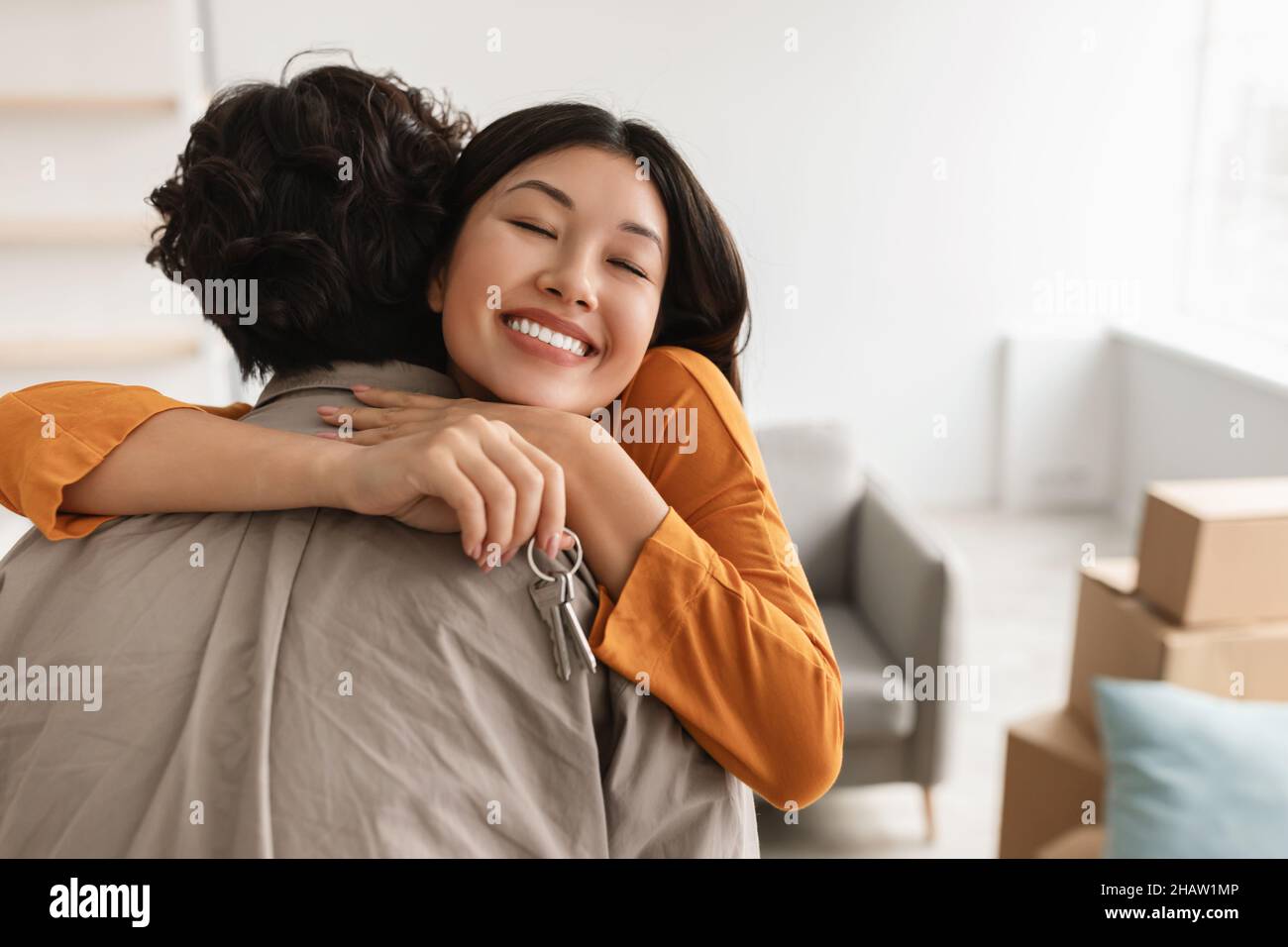 Young Asian lady hugging her husband and holding house key in their new ...