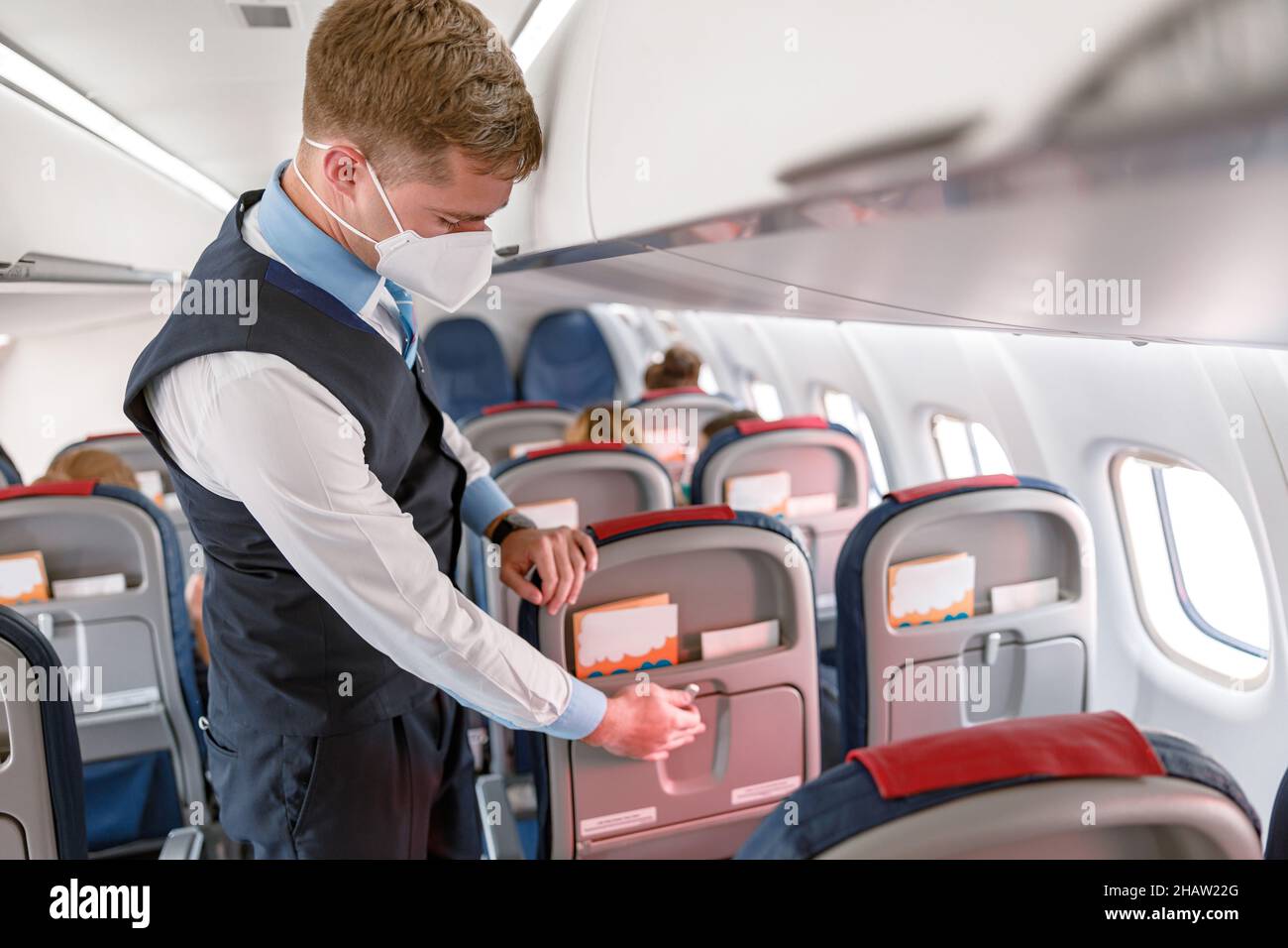 Flight attendant in face mask preparing passenger seat in airplane ...