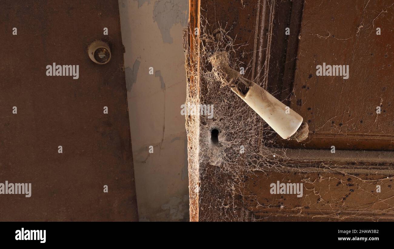Old door with keyhole, hanging door handle and cobwebs, dilapidated ...