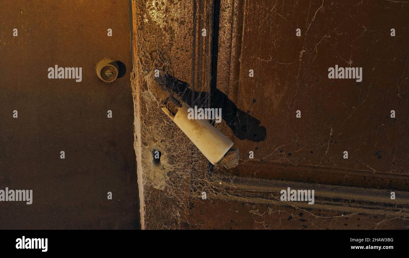 Old door with keyhole, hanging door handle and cobwebs, dilapidated ...