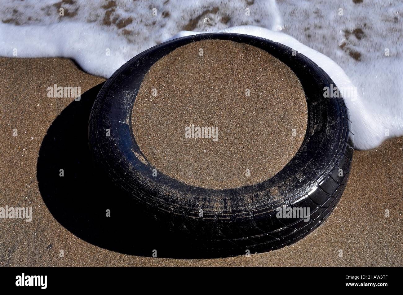 Washed up car tyre on the beach, car tyre filled with sand washed over ...