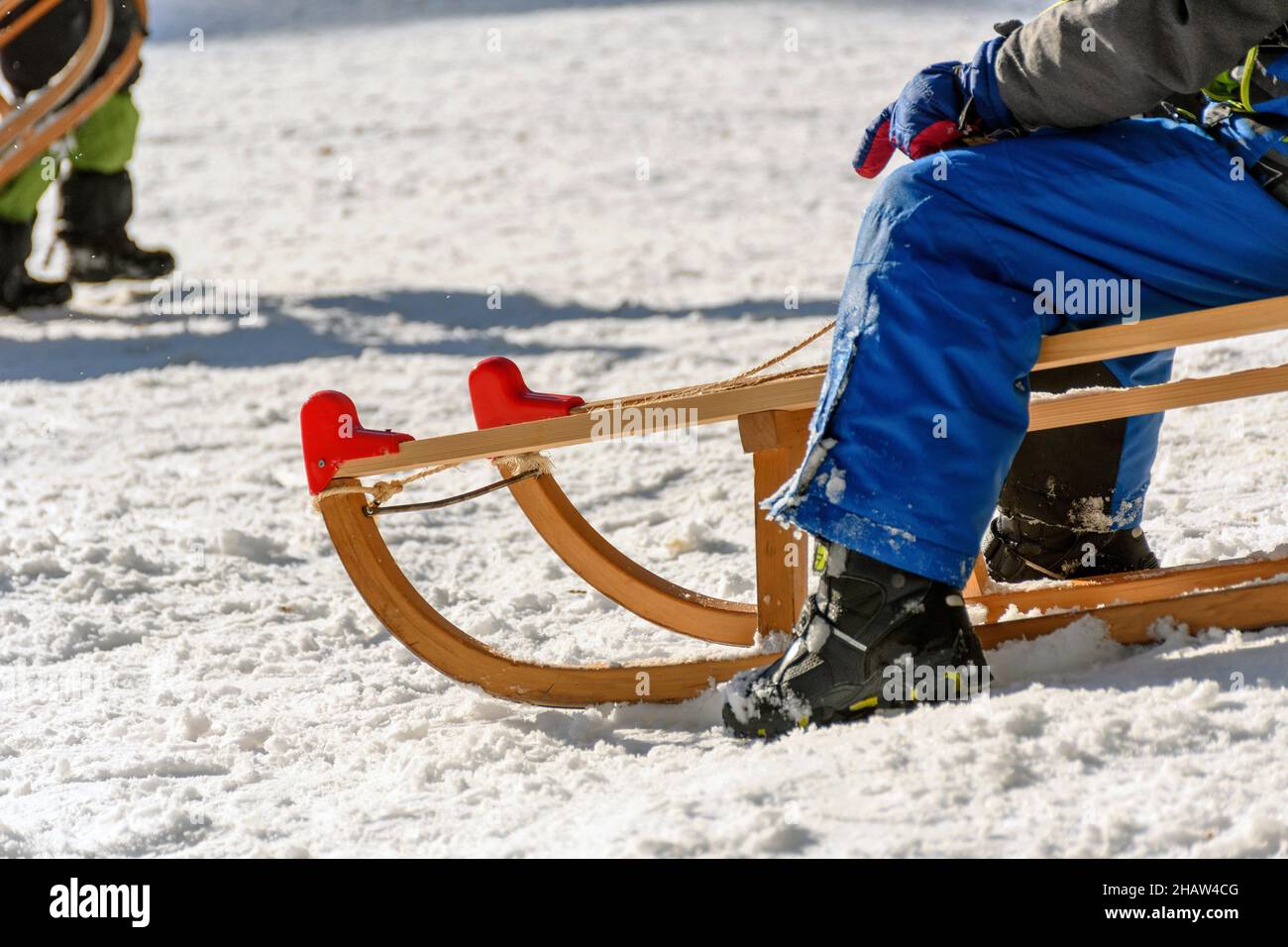 Close-up of child on wooden sled, ready to ride downhill on snowy slope ...