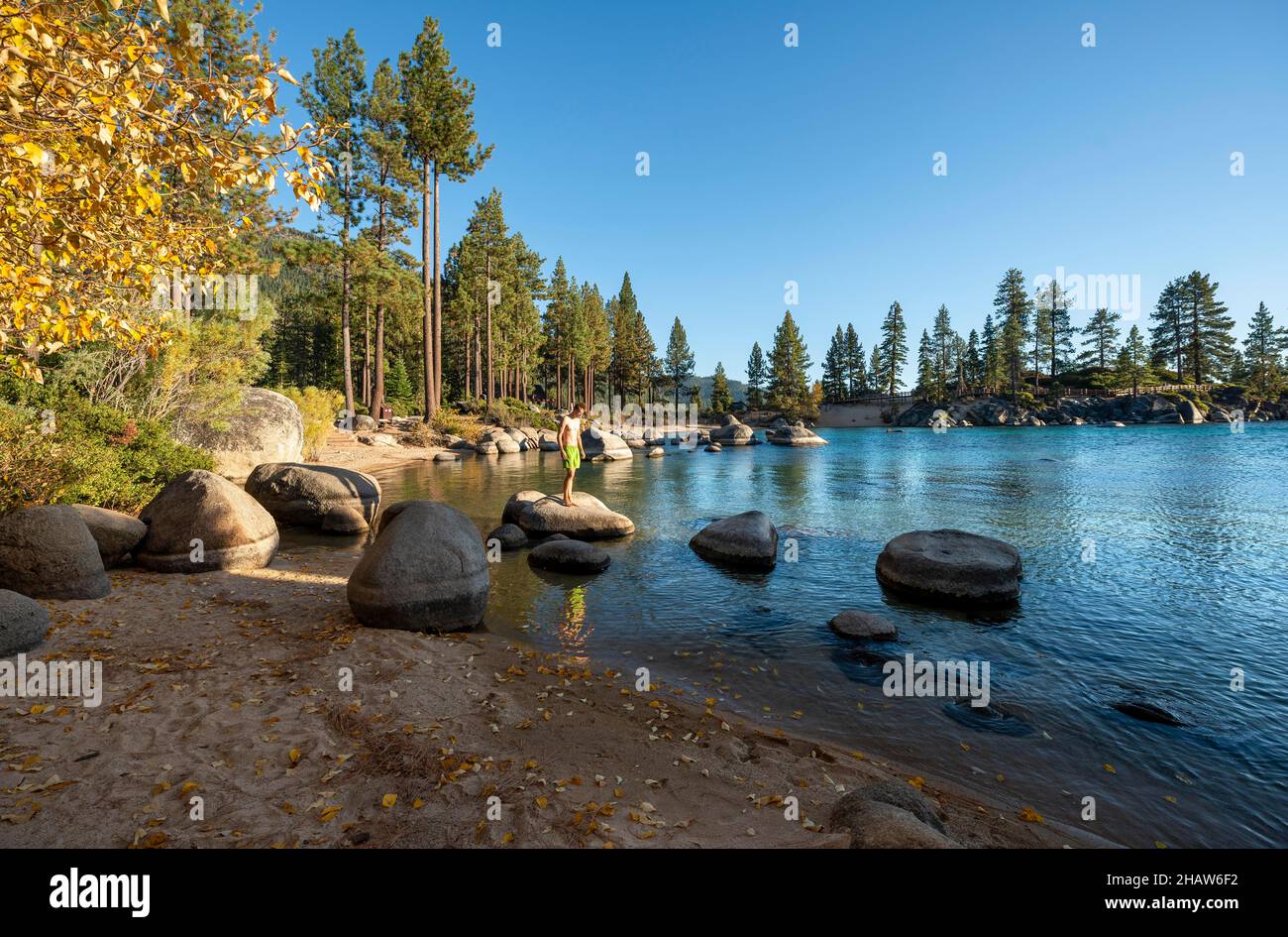 Young man in swimming trunks on round stones in the water, on sandy ...