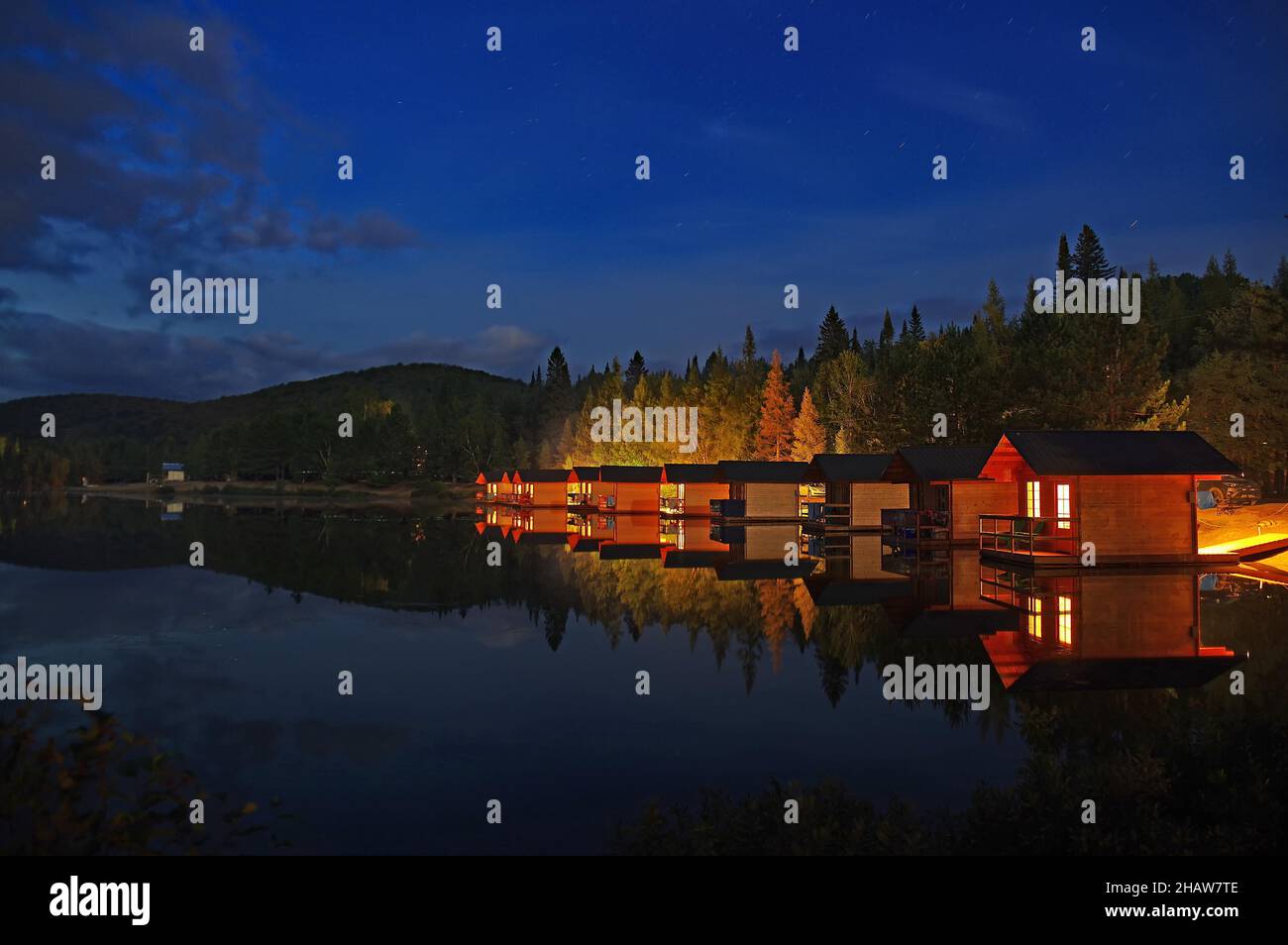 Simple, illuminated wooden cabins reflected in a lake, romantic, Quebec ...