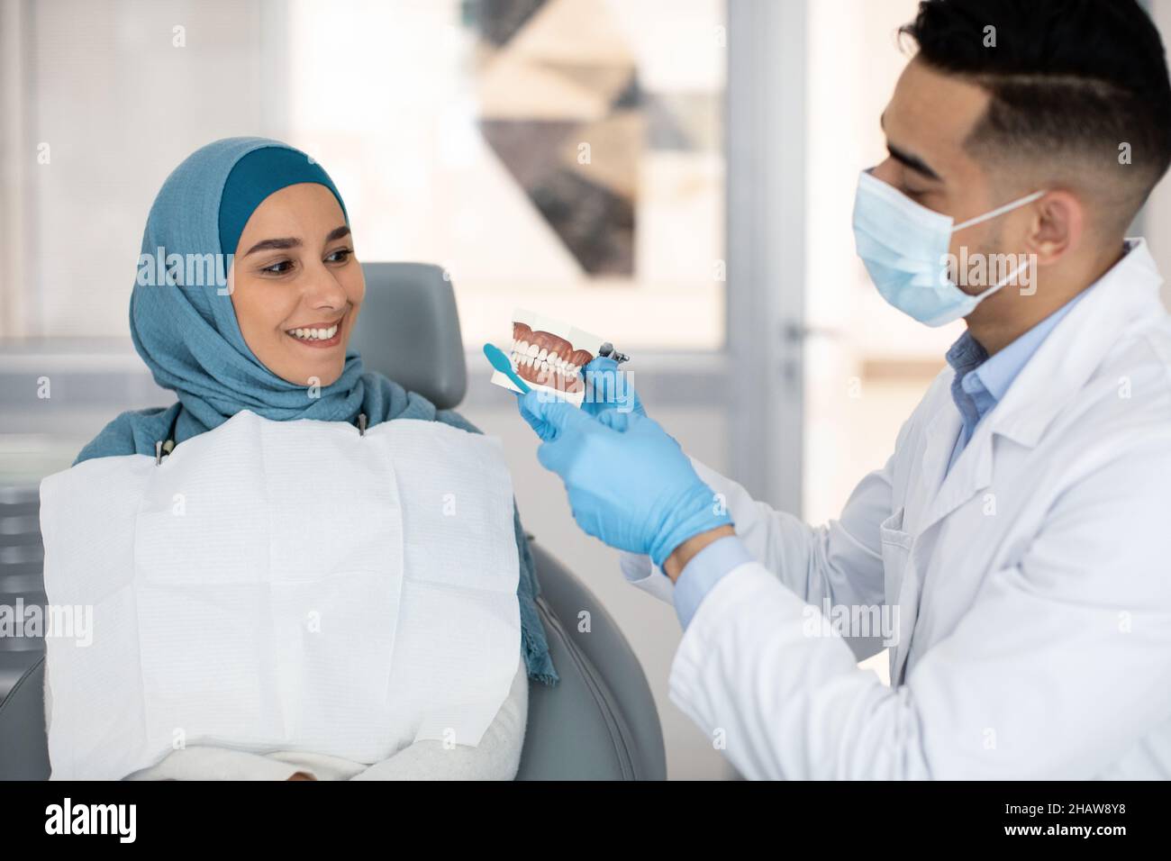 Male dentist holding jaw model, explaining dental hygiene to muslim ...