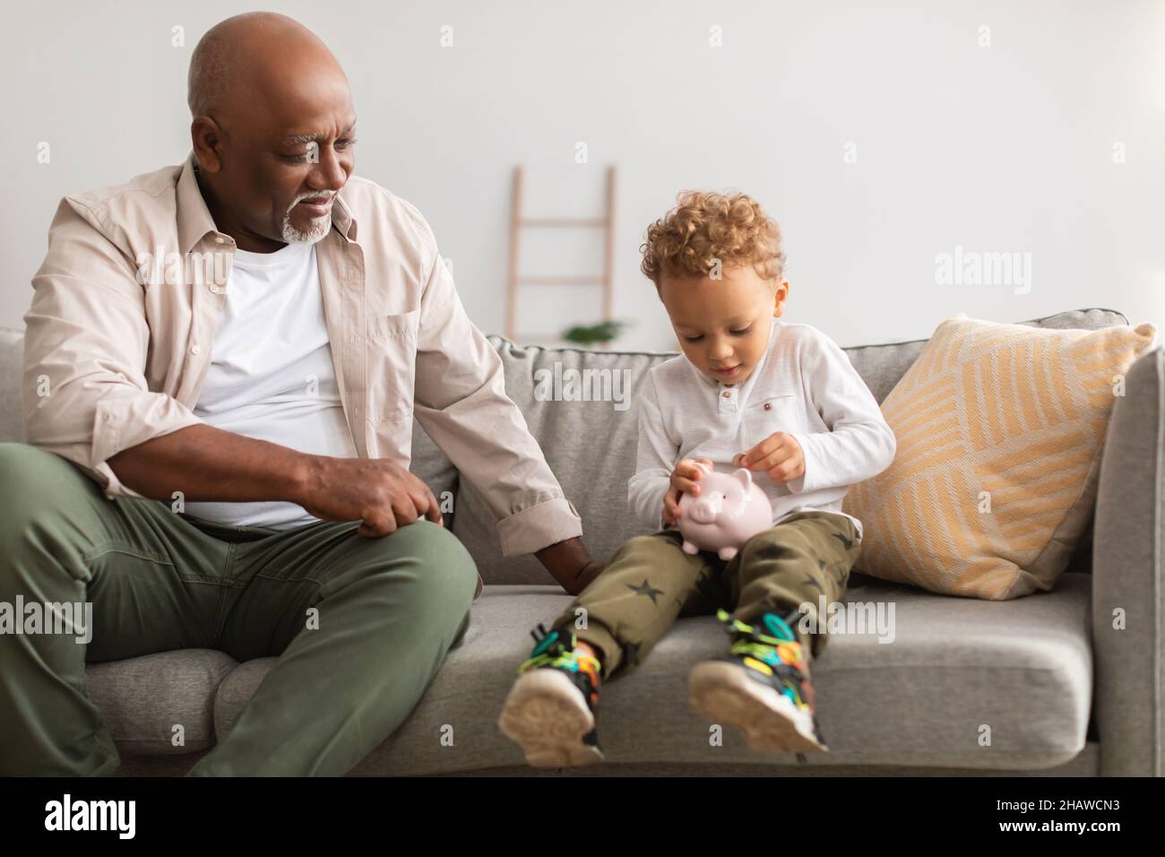 African American Grandpa And Grandson Putting Money In Piggybank Indoor ...