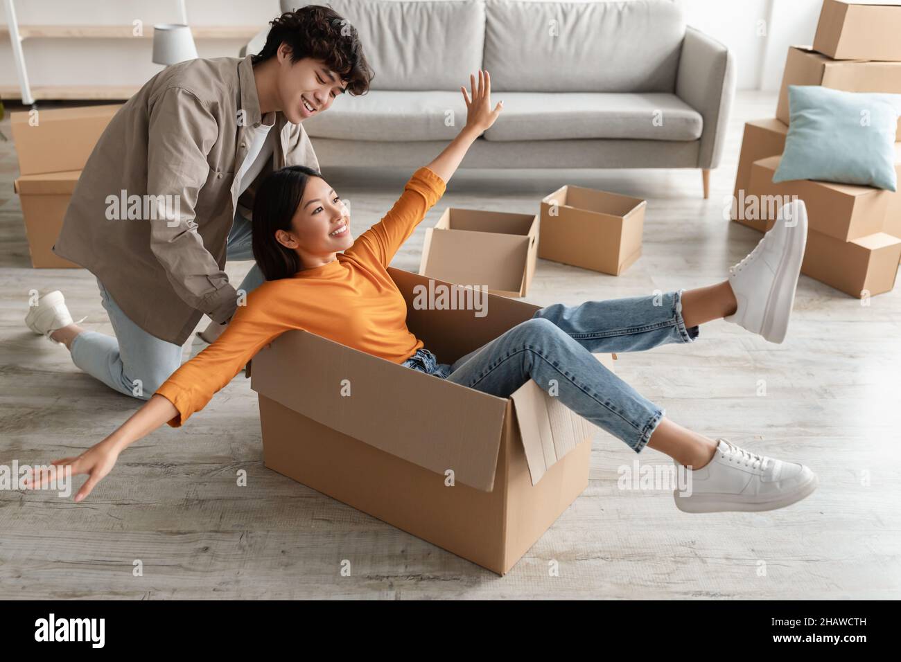 Joyful young Asian couple having fun while unpacking stuff in their new ...