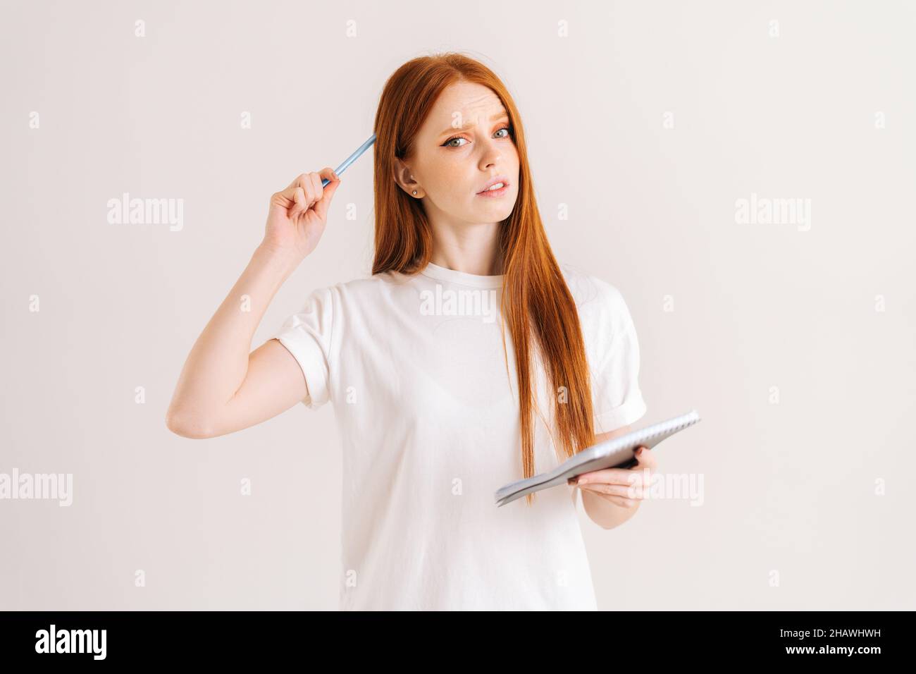 Studio portrait of pondering redhead young woman scratches head with ...