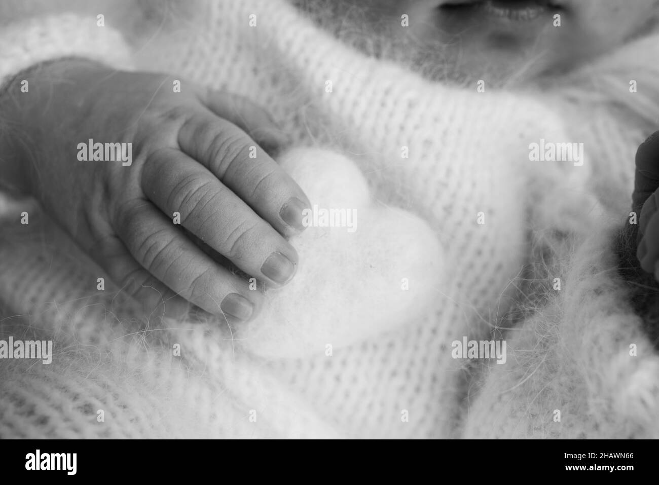 Tiny hand of a newborn baby. Soft hands of new born hold woolen heart ...