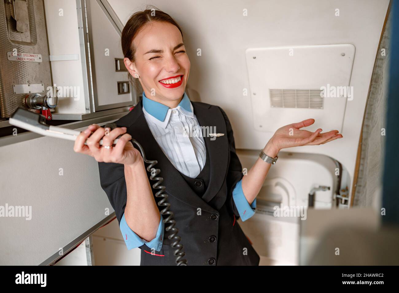 Cheerful flight attendant with telephone standing in aircraft cabin ...