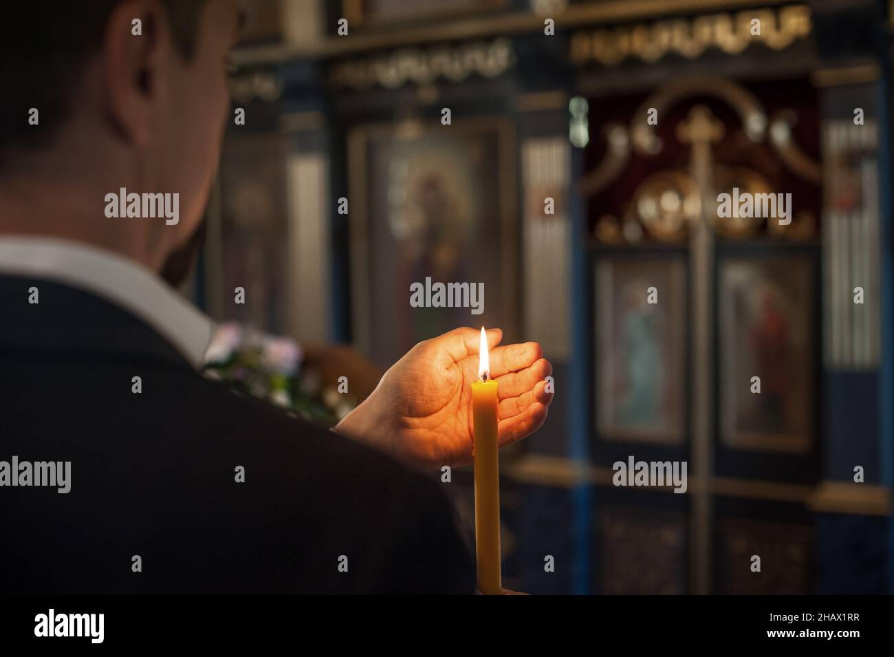 Closeup of hands of religious man holding lit candle and praying in the ...