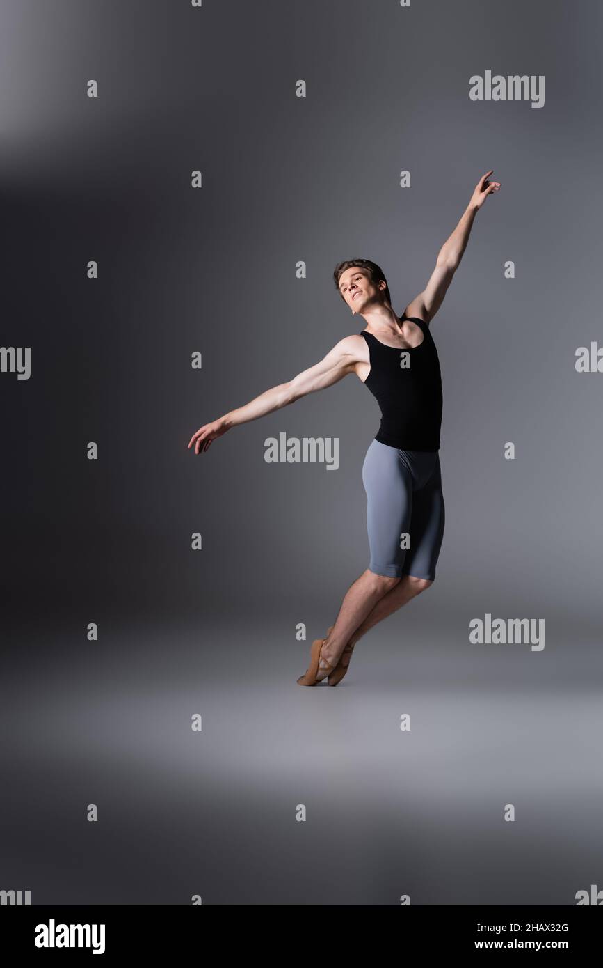 graceful dancer with outstretched hands performing ballet dance on dark ...