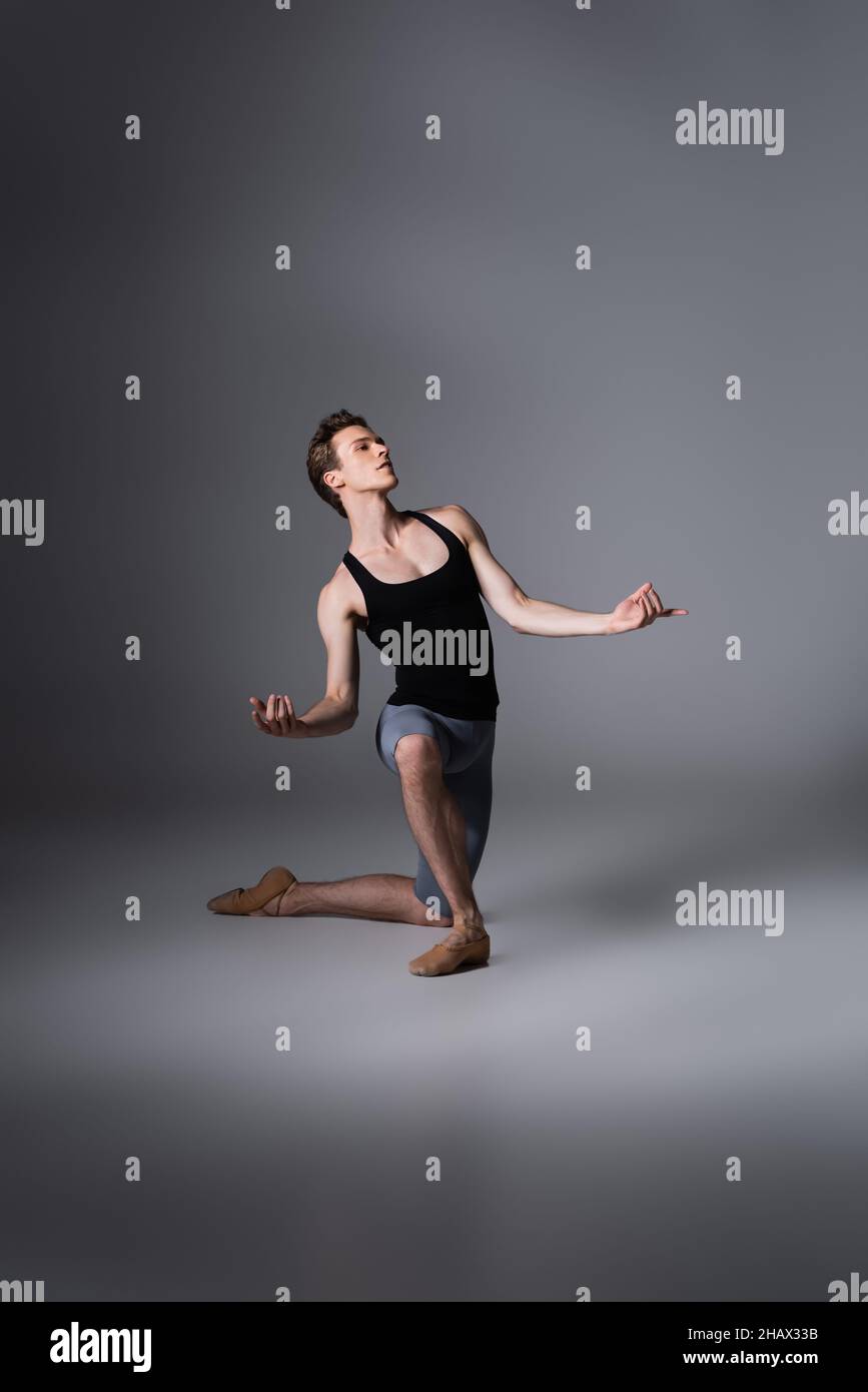 full length of elegant ballet dancer standing on knee while performing ...