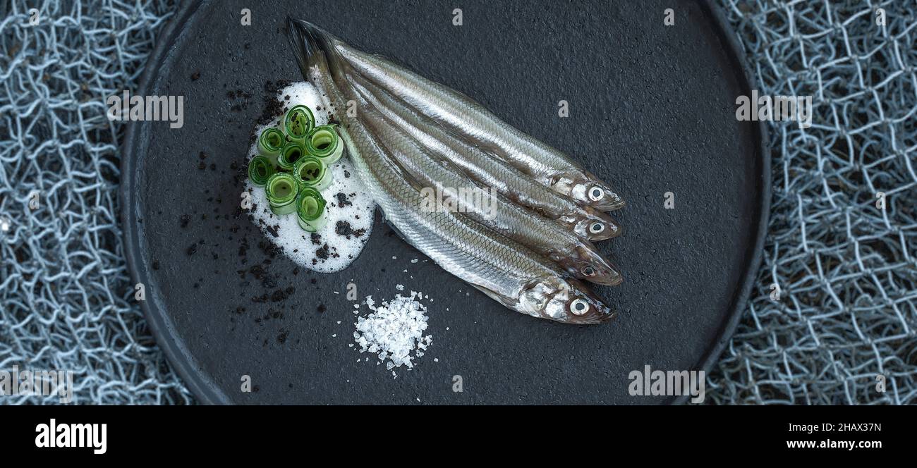 European smelt raw uncooked fish in black craft plate on fishing net ...