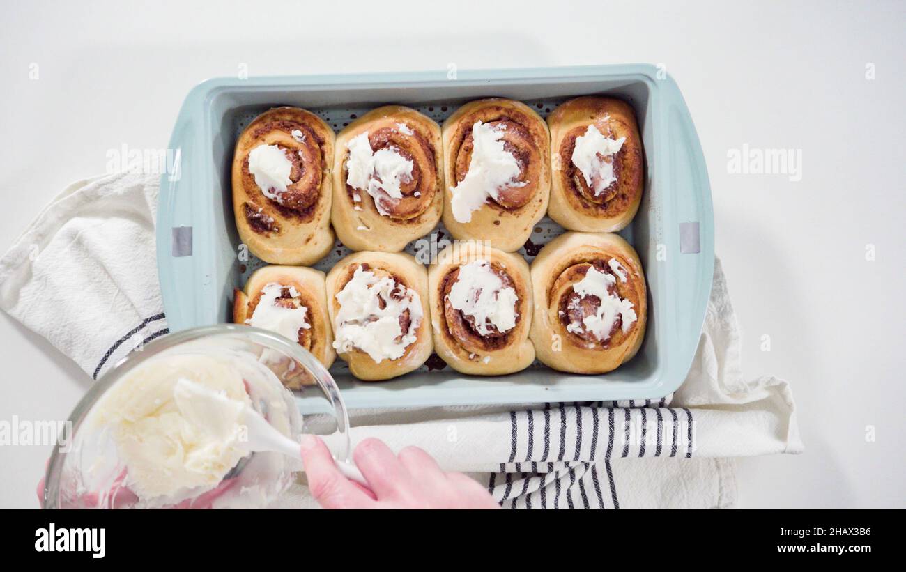 Flat lay. Glazing freshly baked cinnamon rolls in a blue baking pan ...