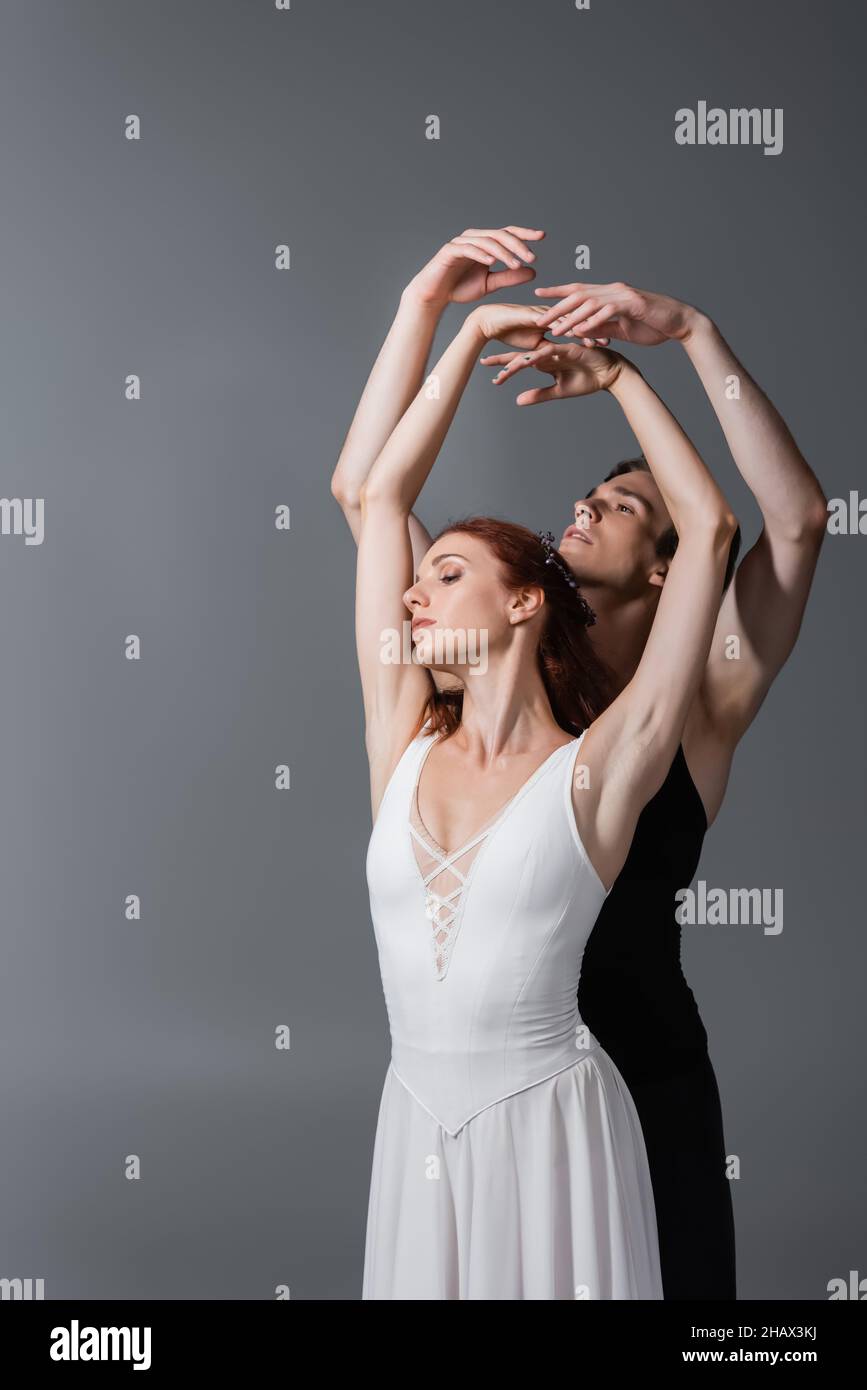 graceful ballerina in white dress dancing with partner while raising ...