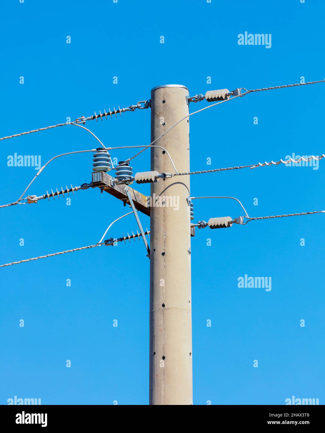 Photograph of a concrete telephone post and cables against a blue sky ...