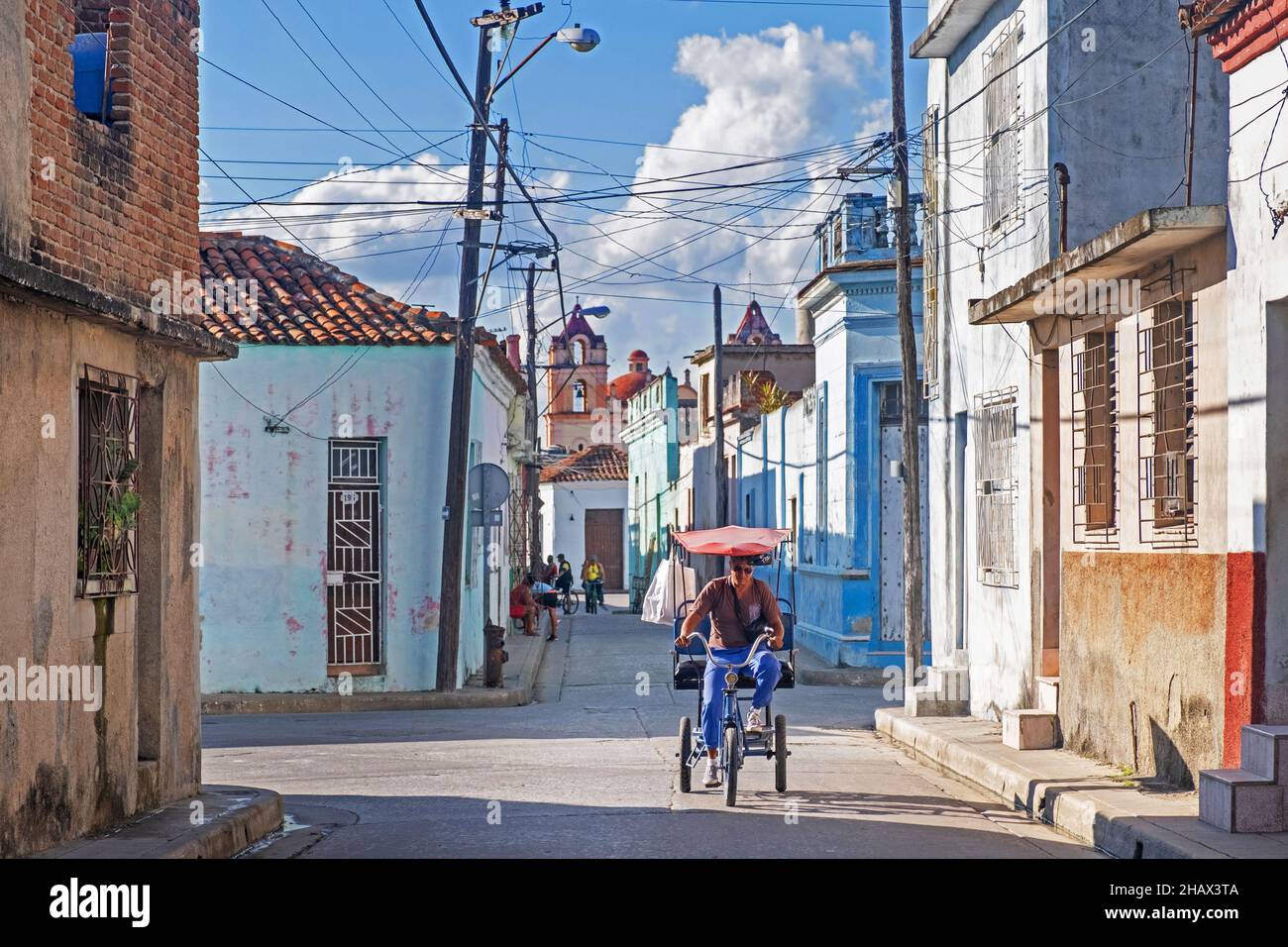 Bicitaxi / bike taxi cycling through narrow street with colourful ...