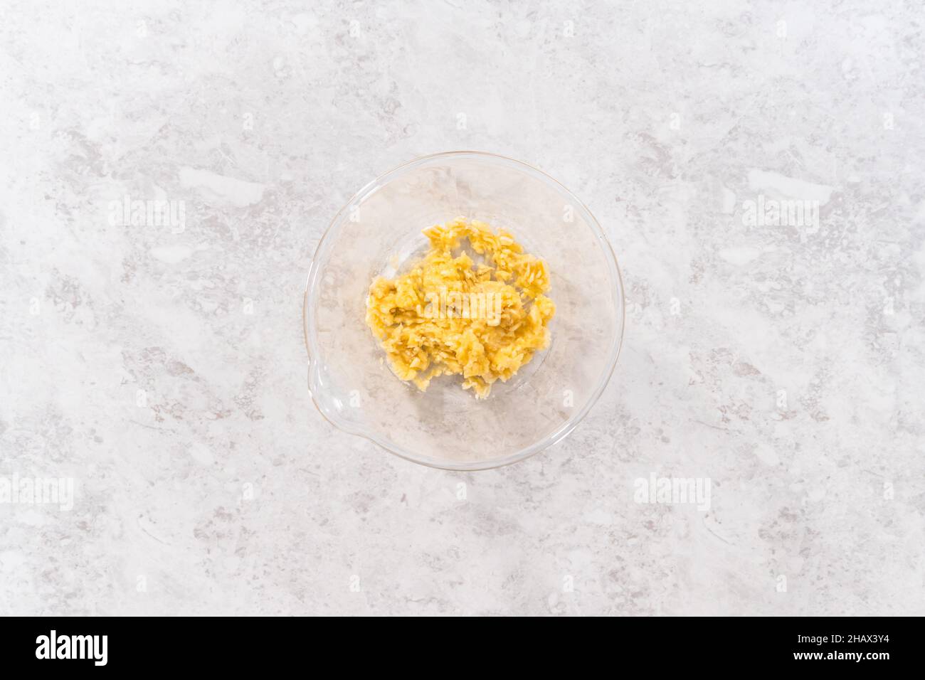 Smashing riped bananas in a glass mixing bowl to prepare coconut banana ...