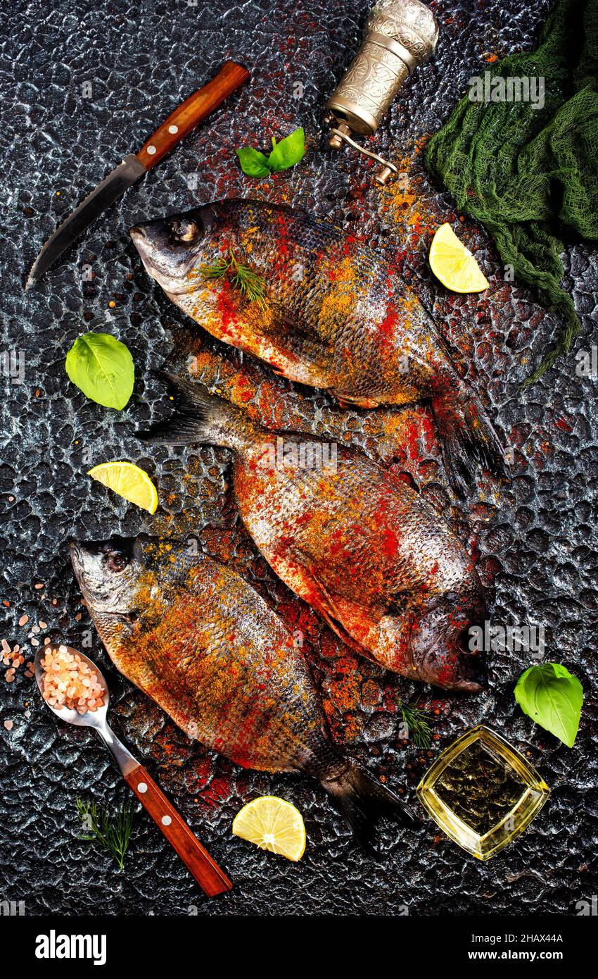 Raw fish with herbs, lemon and olive oil on dark textured background ...
