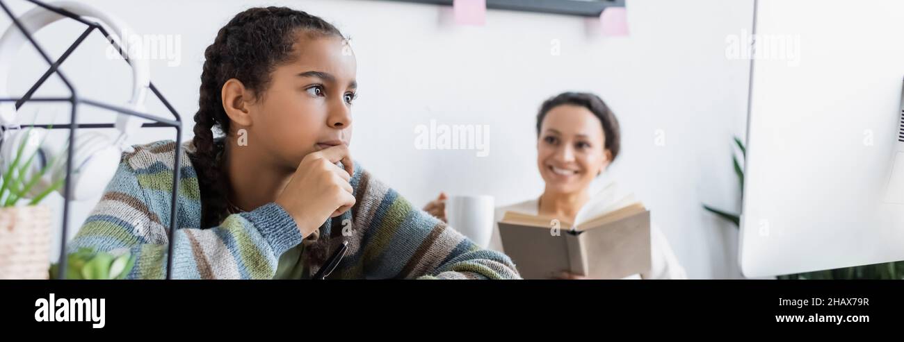 african american teen girl thinking near computer monitor and smiling ...