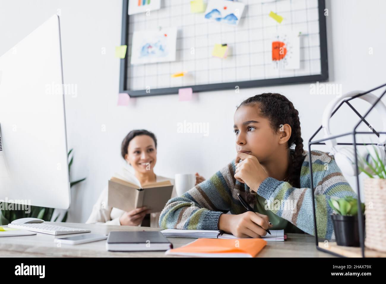thoughtful african american girl doing homework near laptop and mom ...