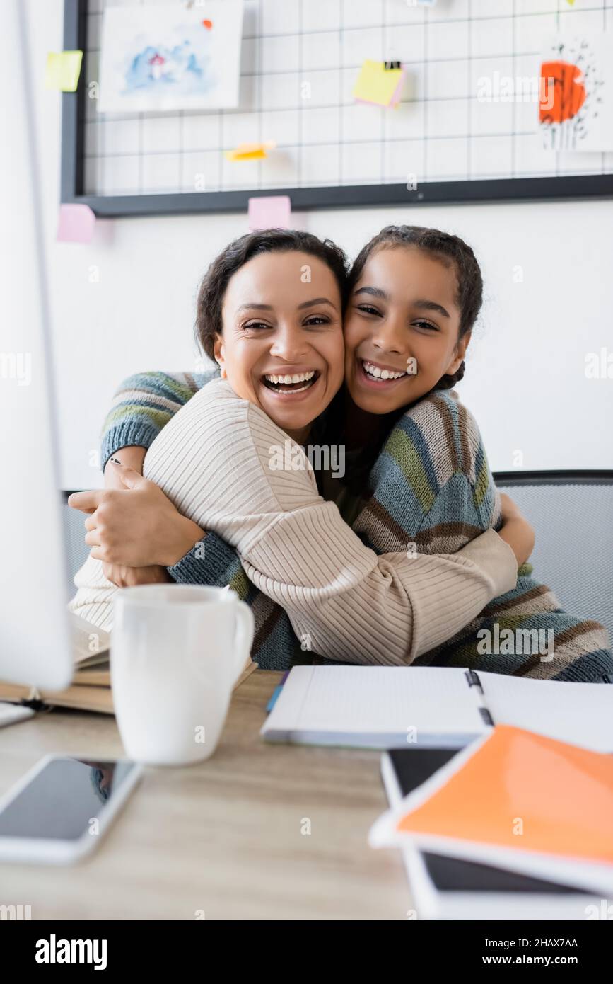 happy african american mother and daughter embracing near blurred computer at home Stock Photo ...