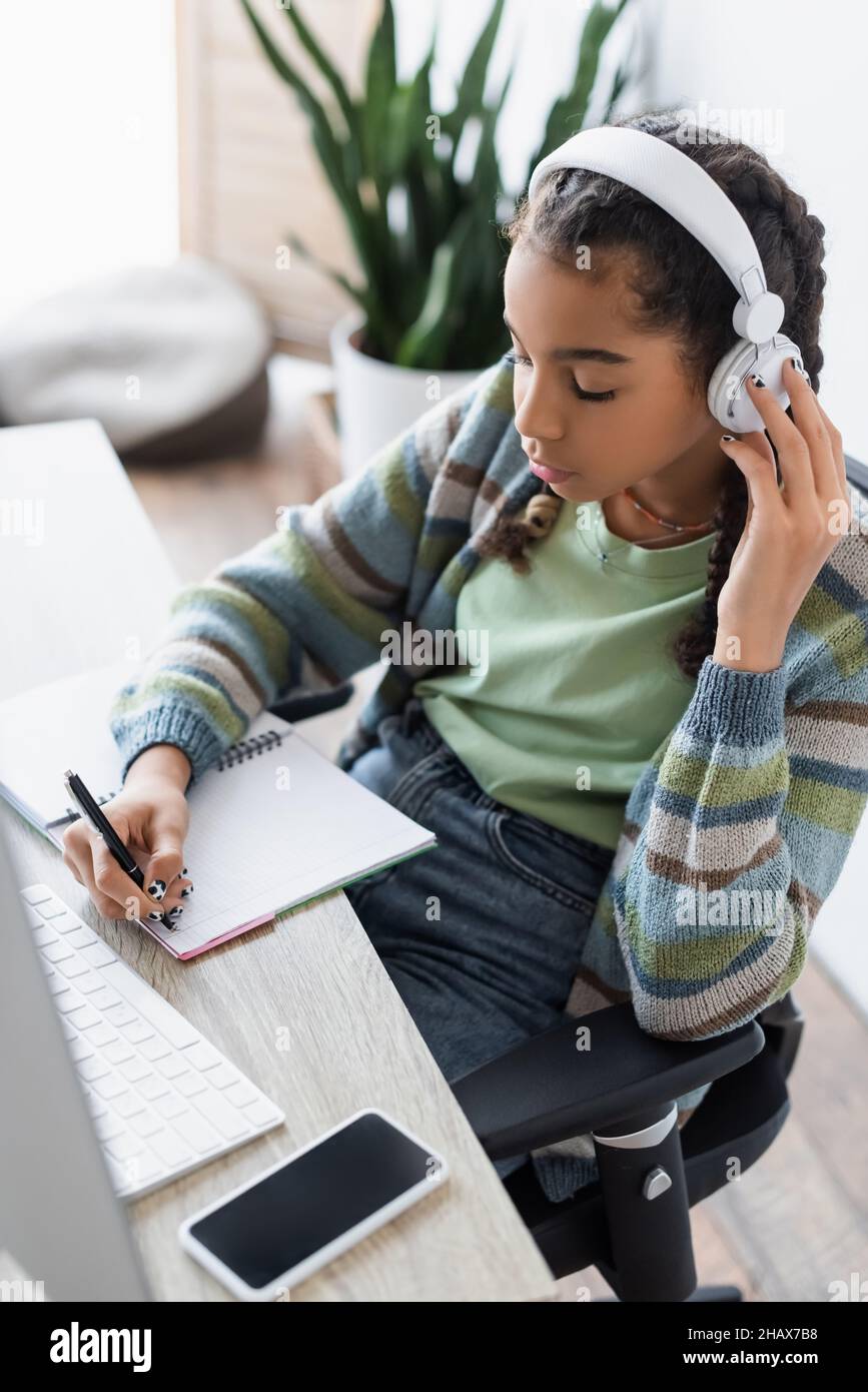 african american teenager writing in notebook while listening audio ...