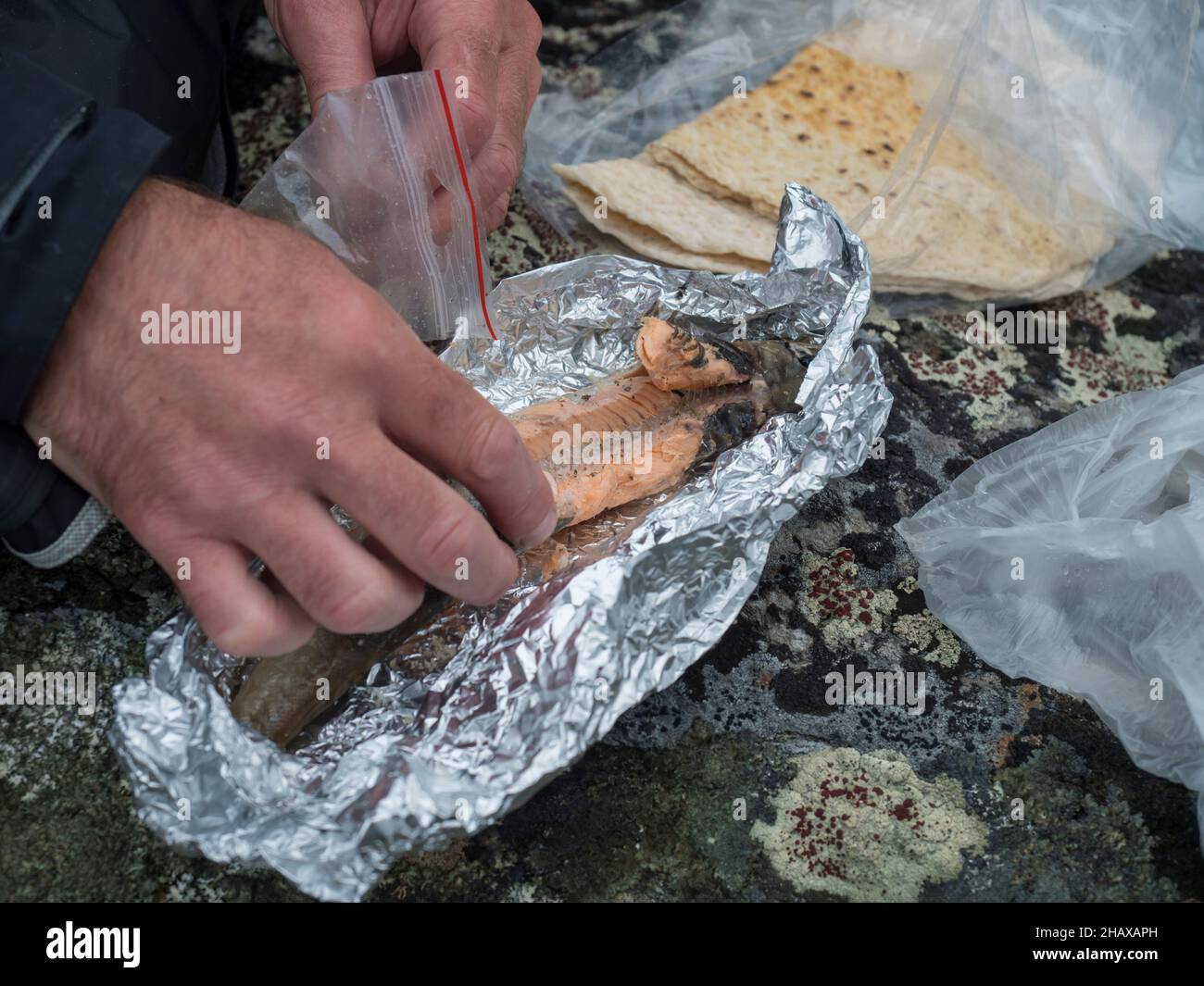 Man hands eating freshly smoked brown trout in tinfoil with traditional ...