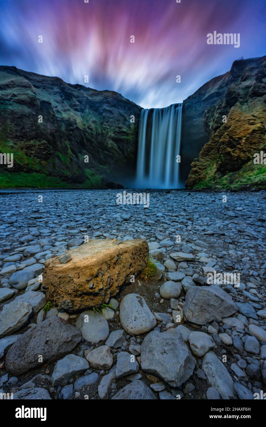 Vertical shot of a scenic waterfall against a colorful sky at dusk ...