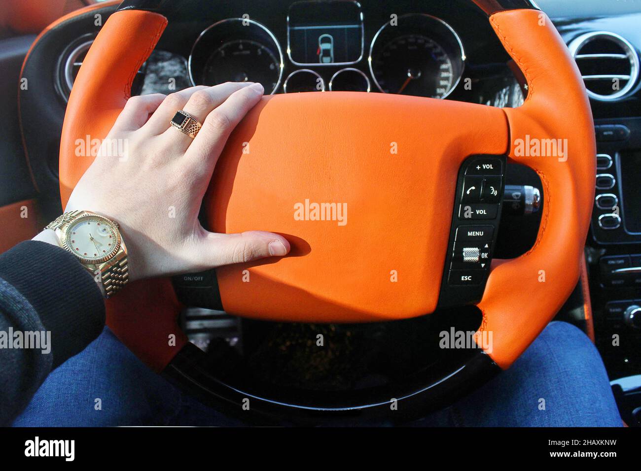 A man holds the steering wheel of a luxury car. Gold watch and a ring ...