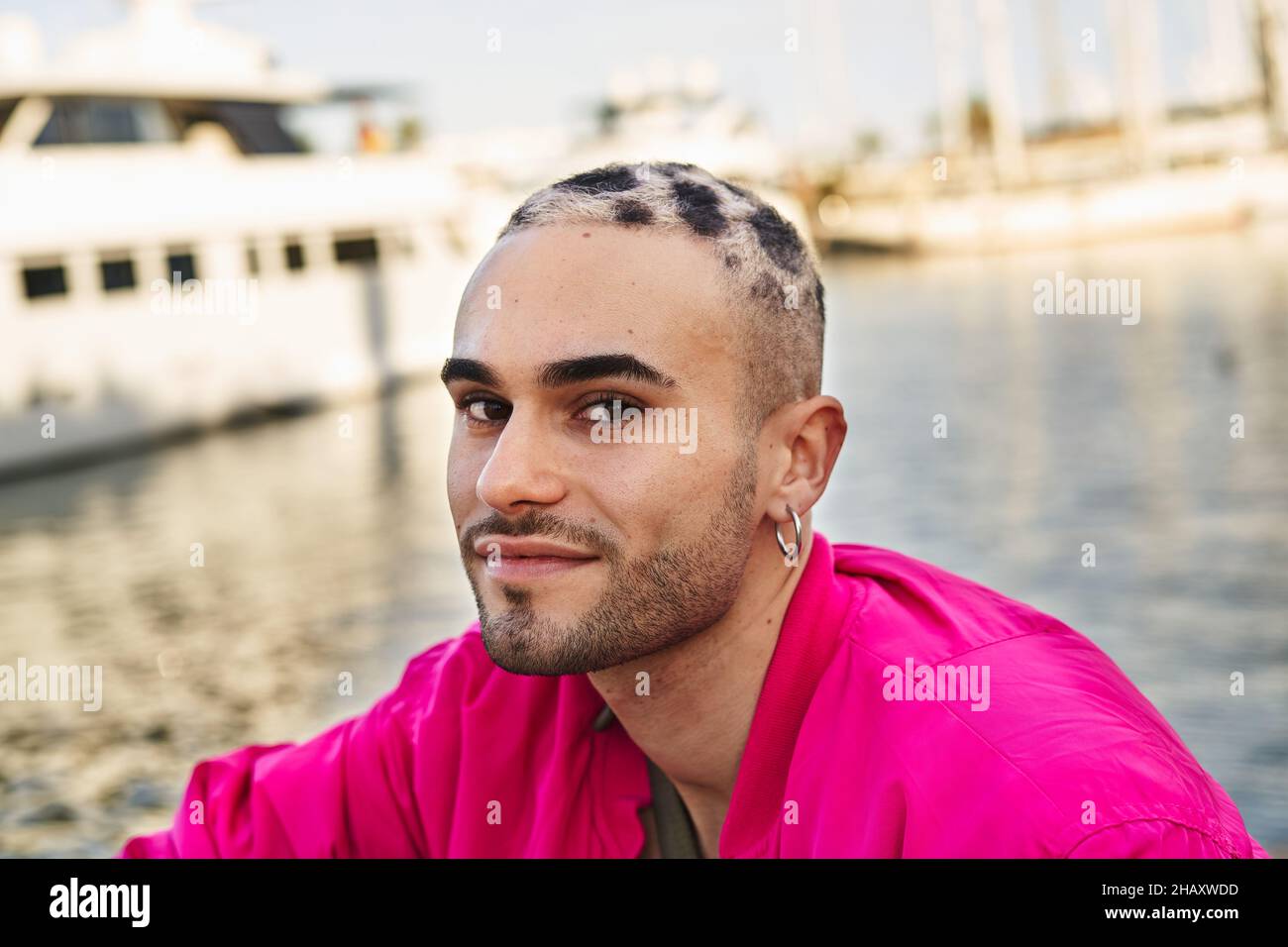 Eccentric young male with unusual haircut sitting on marina with yachts ...