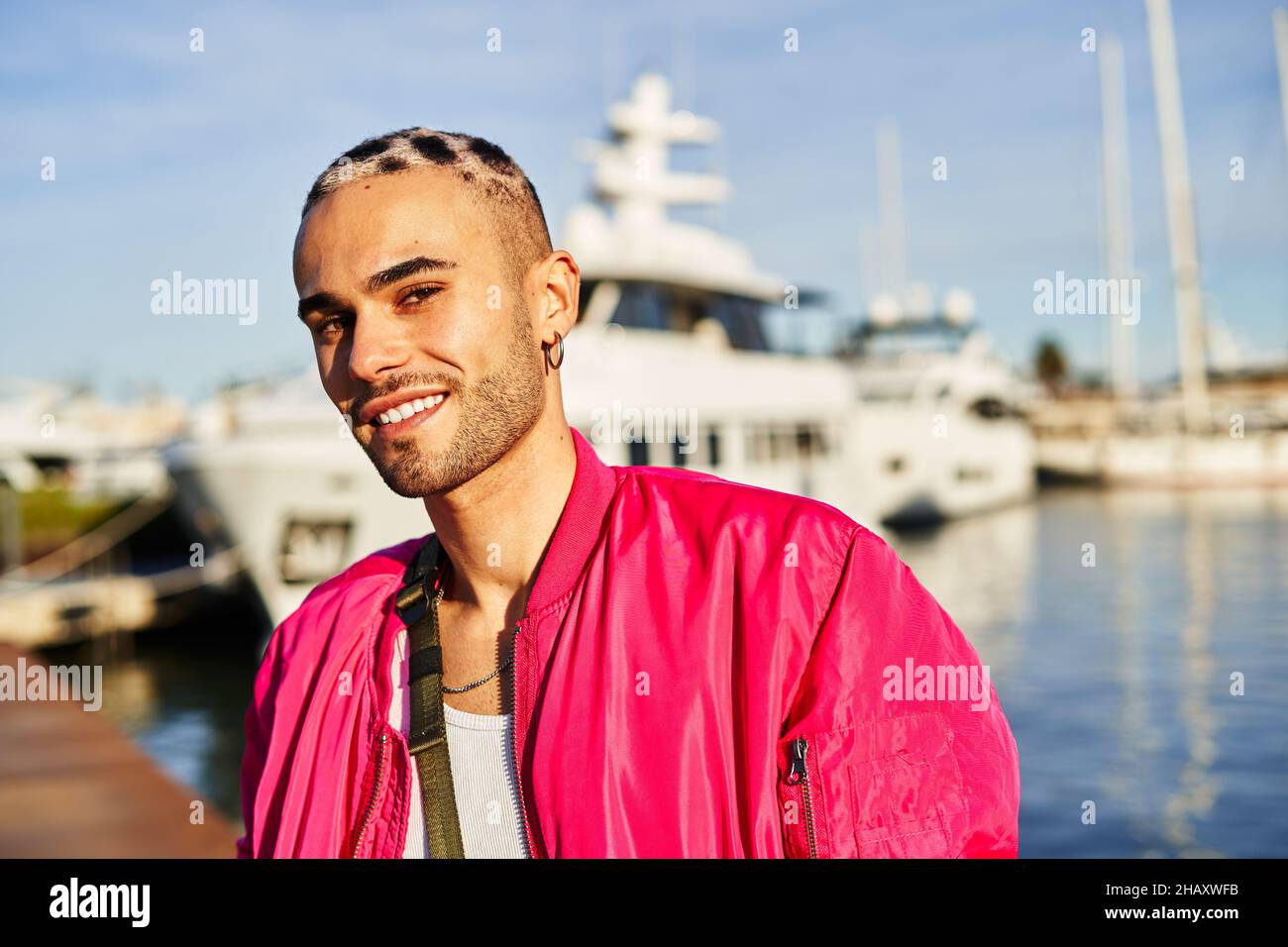 Eccentric young male with unusual haircut sitting on marina with yachts ...