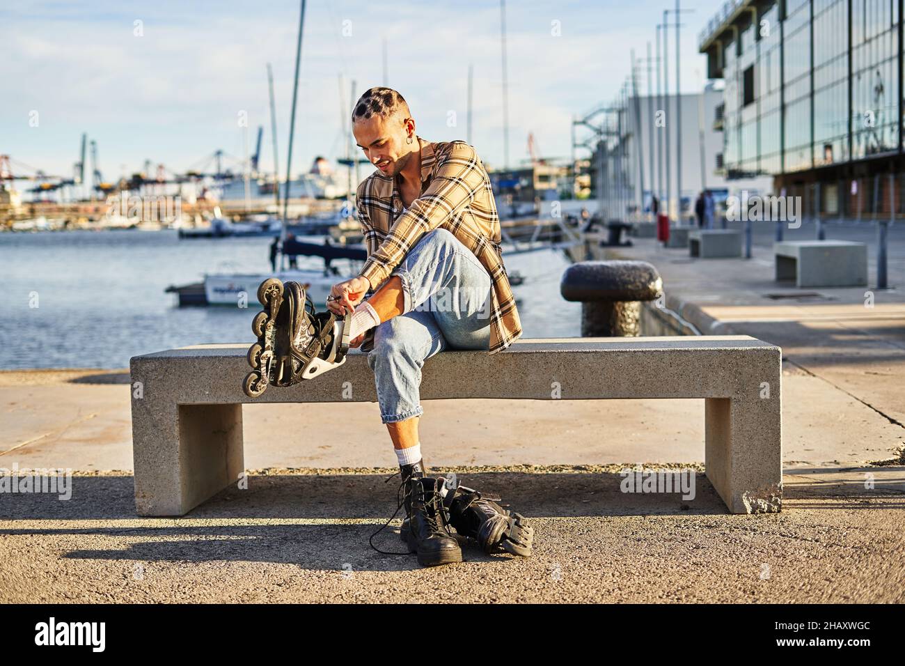 Full body of eccentric male sitting on bench and putting on roller ...