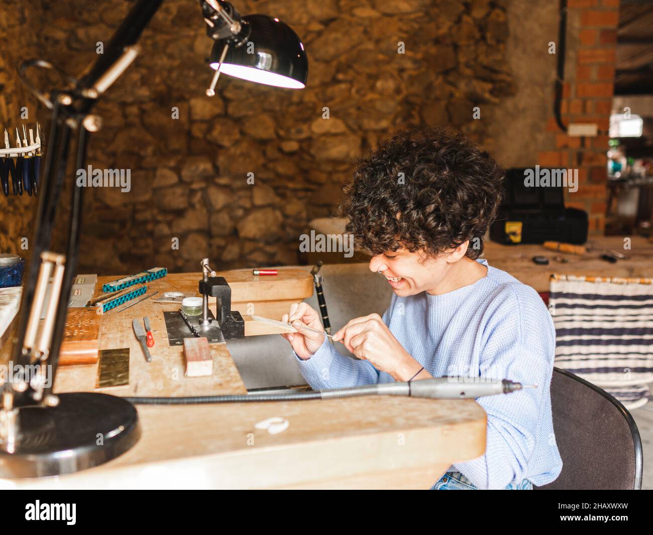 Side view of Hispanic curly female goldsmith using polishing tool while ...