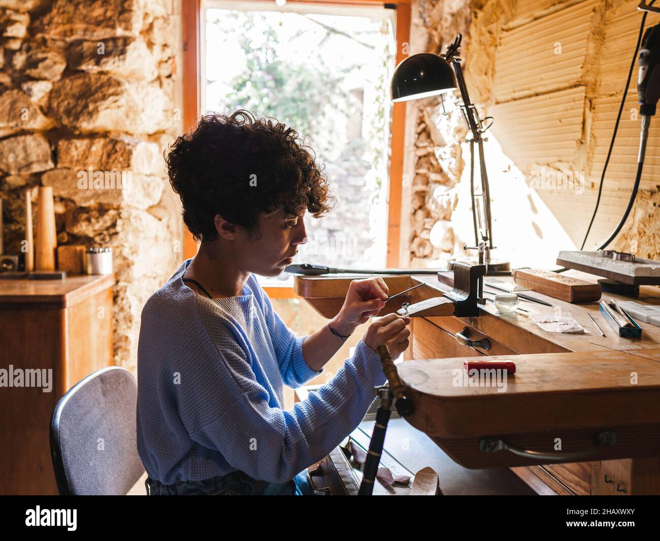 Side view of Hispanic curly female goldsmith using polishing tool while ...