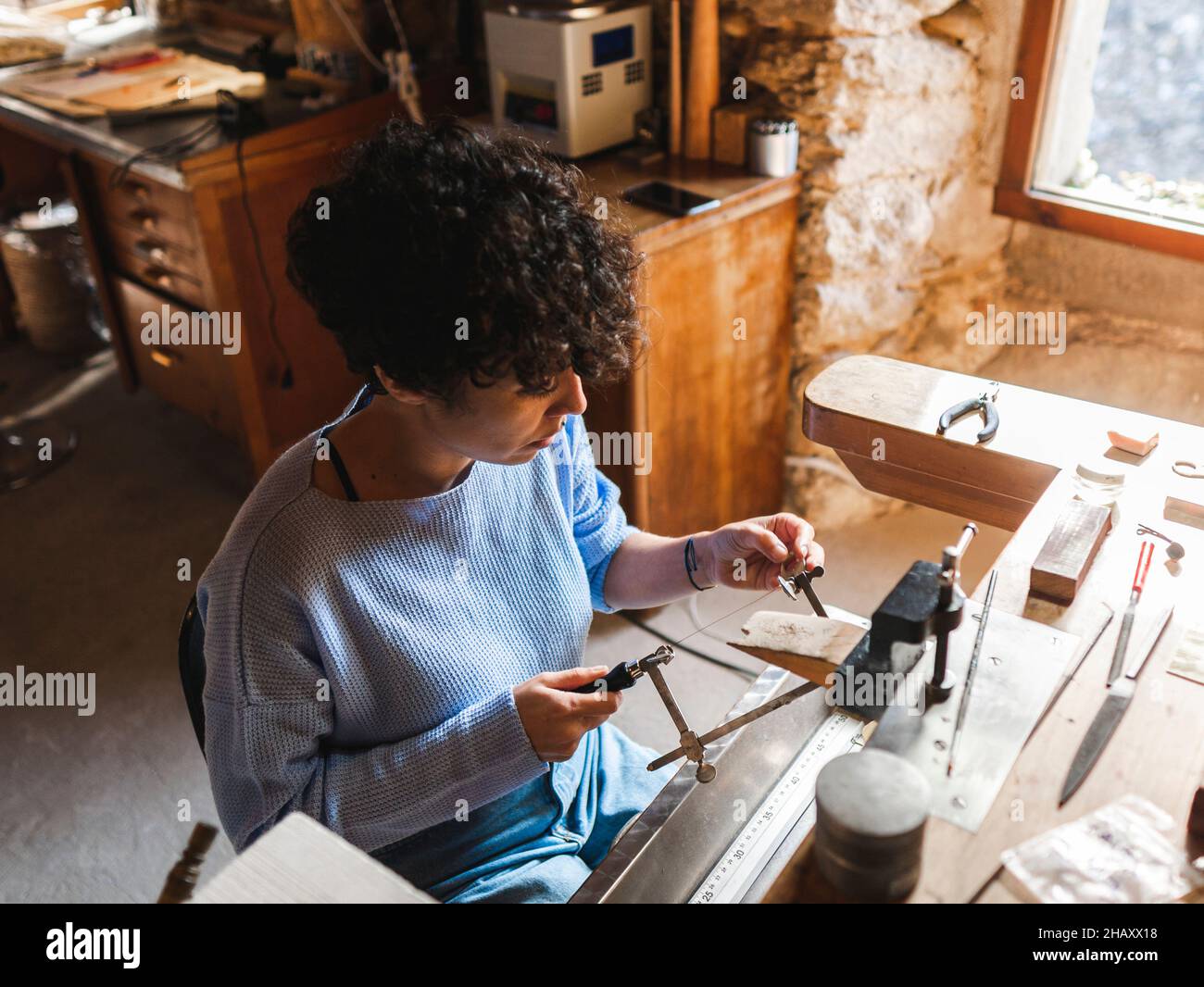 Focused Hispanic female goldsmith master using manual fretsaw while ...