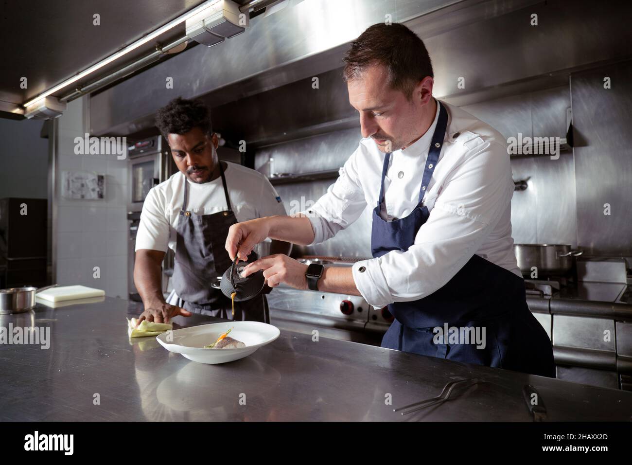 Focused male cook adding bouillon from ceramic pot to fish while ...