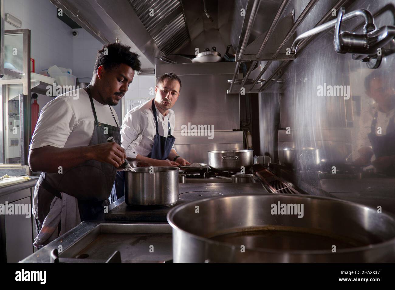 Concentrated black cook mixing food in steel pot with chef explaining ...