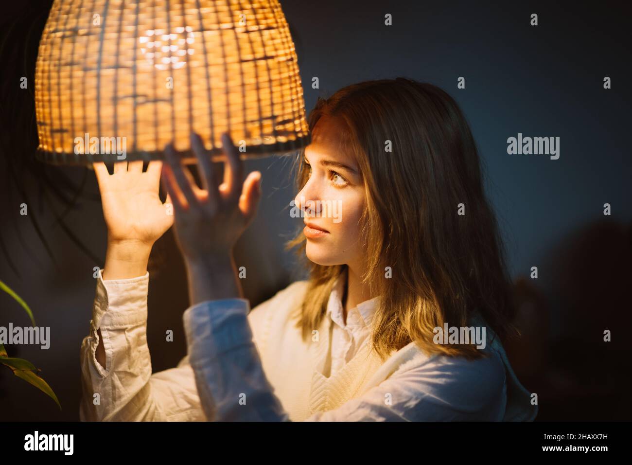 Side view of young female holding lampshade of illuminated chandelier ...