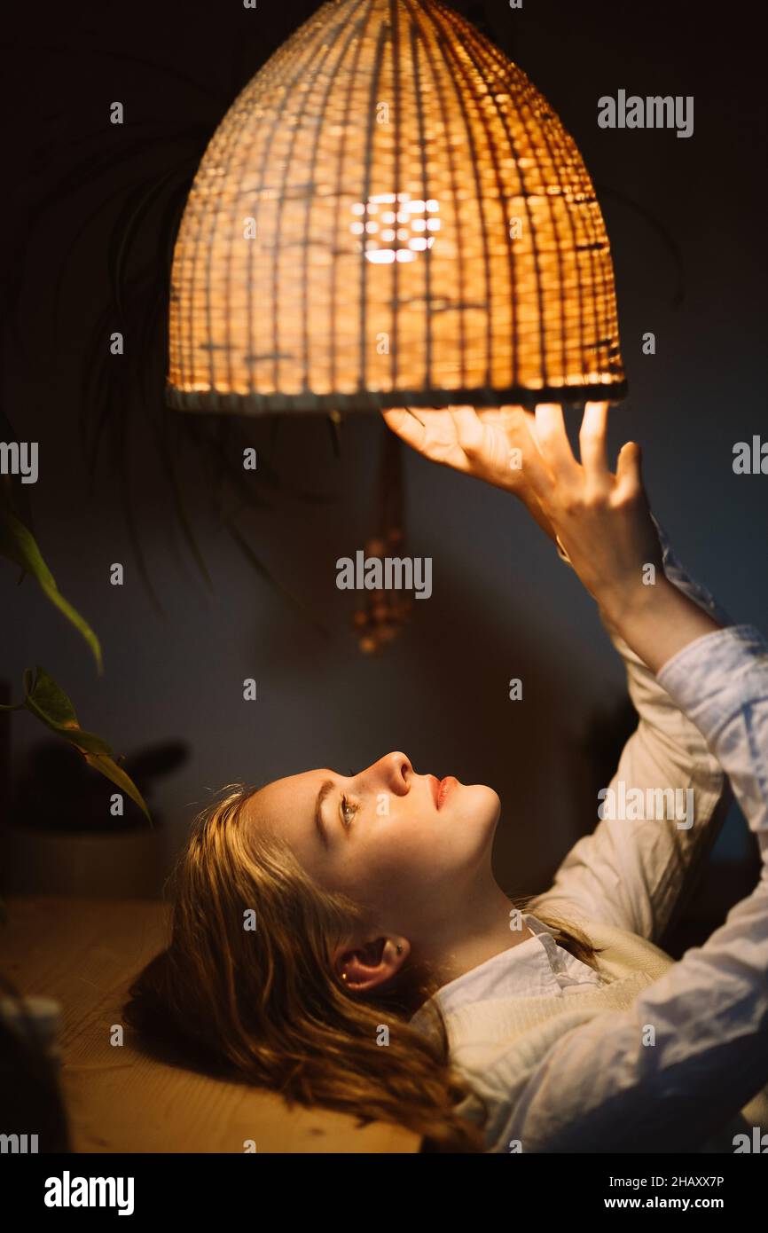 Side view of young female lying under illuminated lamp of chandelier ...