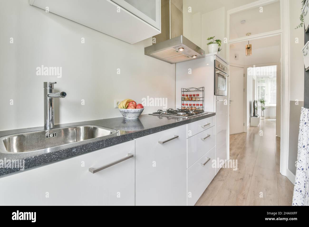 Interior of modern light narrow kitchen furnished with white cupboards ...