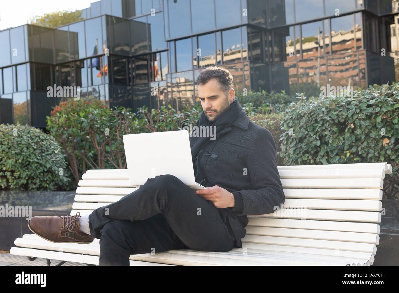 Pensive male entrepreneur in casual clothes sitting on wooden bench and ...