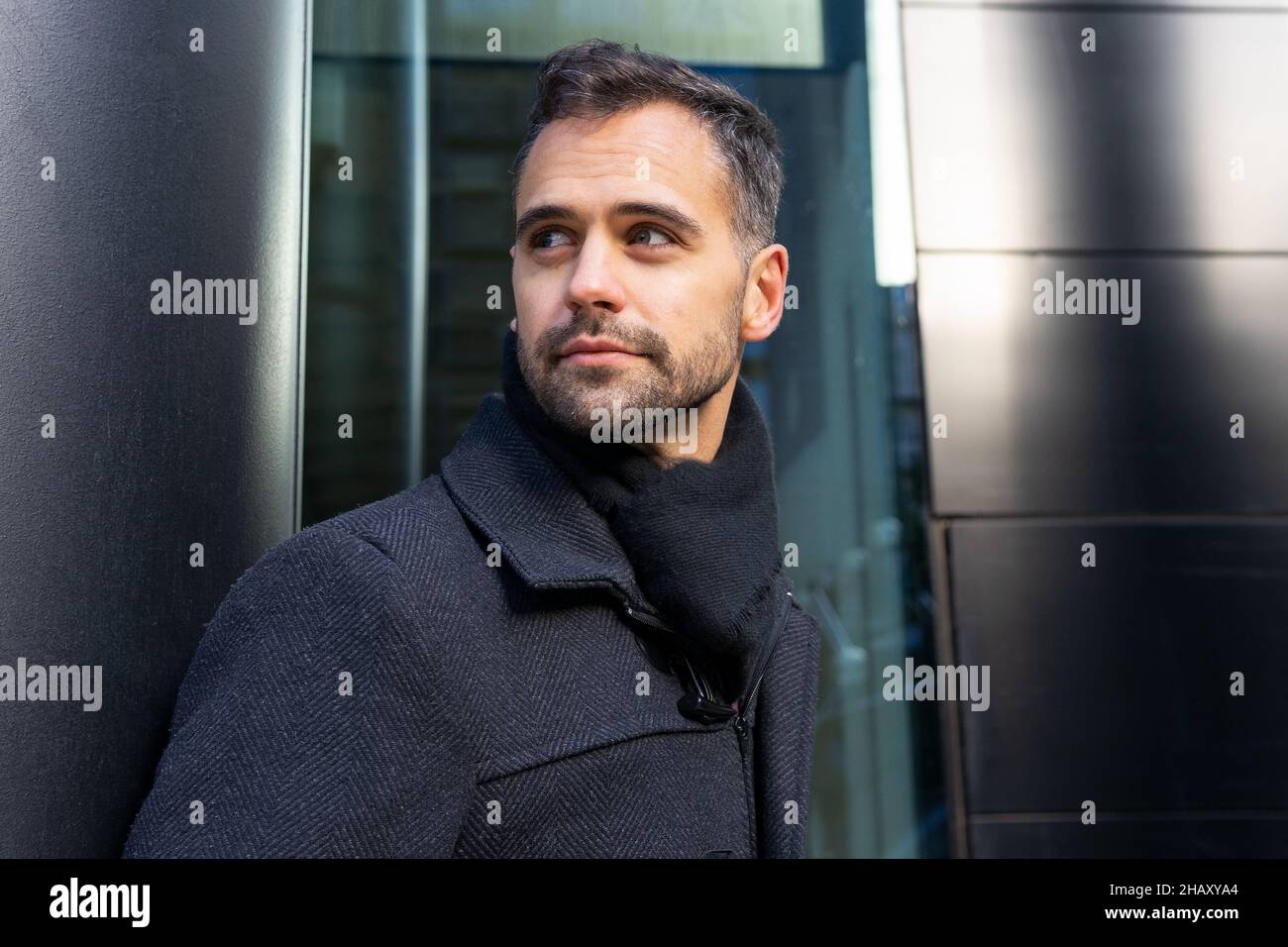 Serious male in black coat standing on street near column of ...