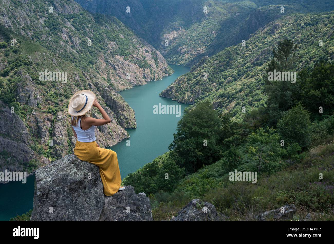 Back view of anonymous traveler Woman sitting on edge of rocky mountain ...