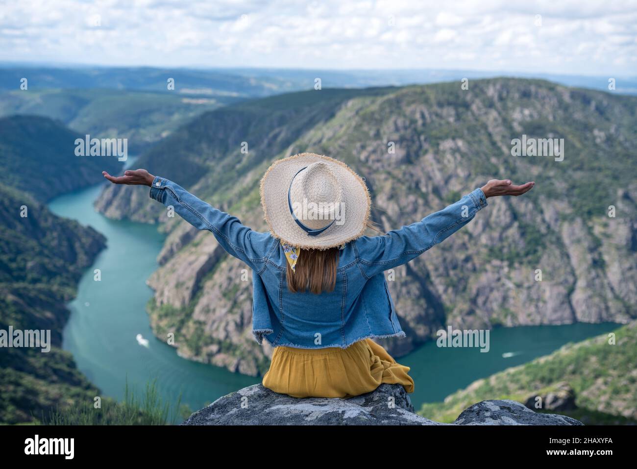 Back view of anonymous traveler Woman sitting on edge of rocky mountain ...