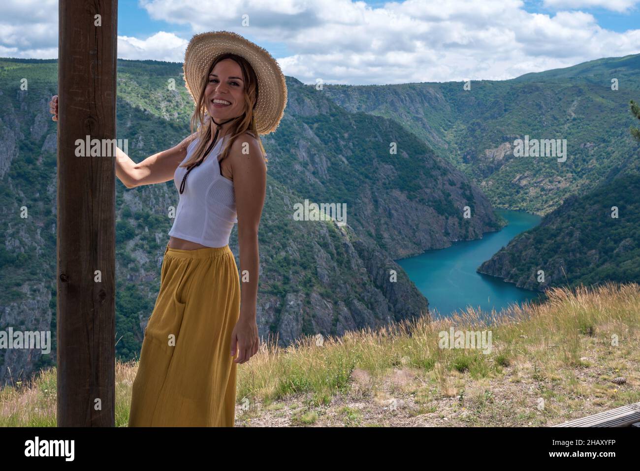 Side view of young female traveler in straw hat leaning on wooden ...